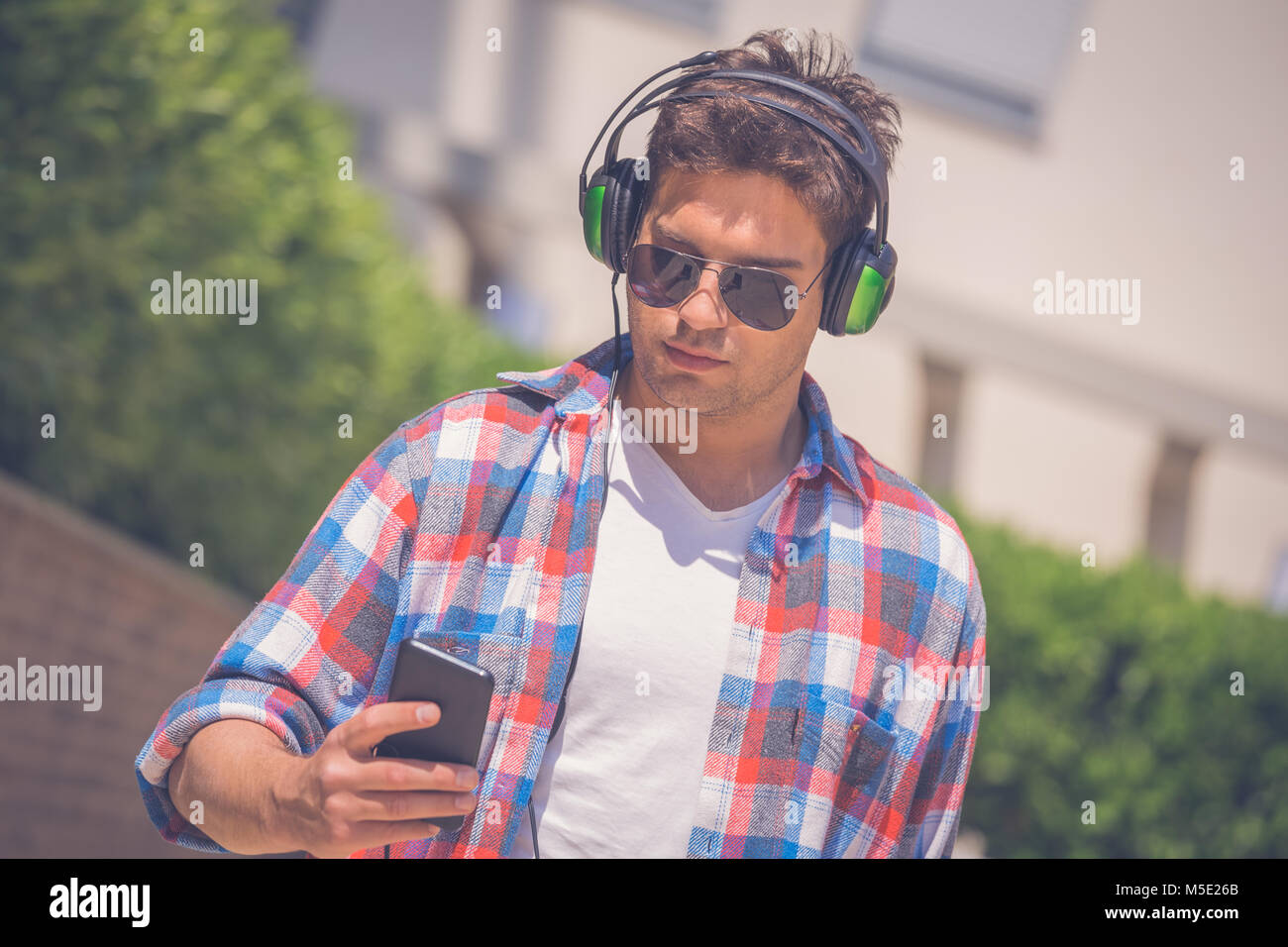 Modern fashionable man looking at smartphone and using music player app ...