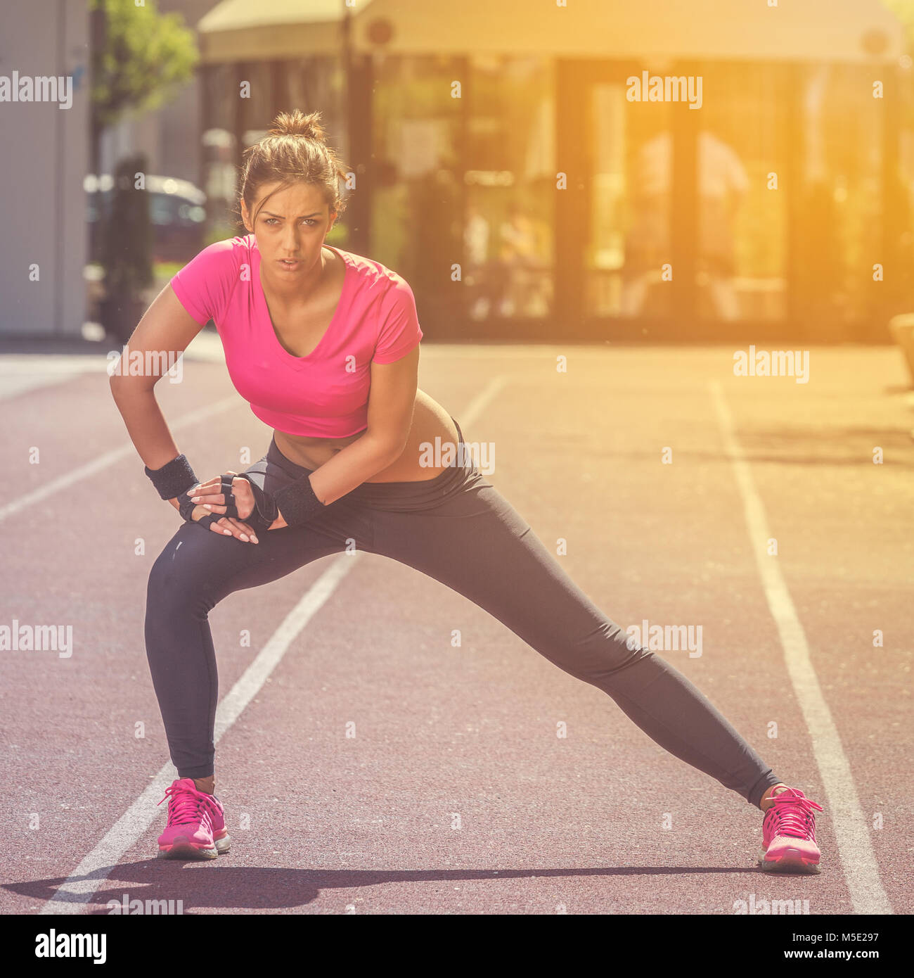 Sportswoman standing on running track and stretching legs before ...