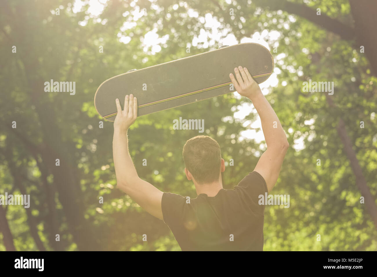 Back view of man holding skateboard in the park. Extreme sports and ...