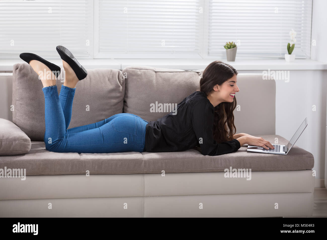 Happy Woman Lying On Couch Using Laptop At Home Stock Photo - Alamy