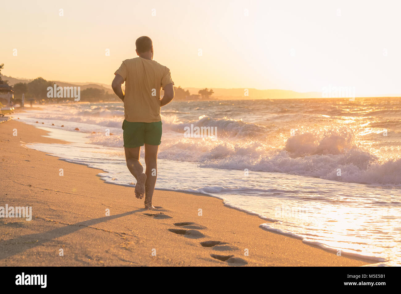 Rear view of young jogger running on beach at sunset over sea Stock ...