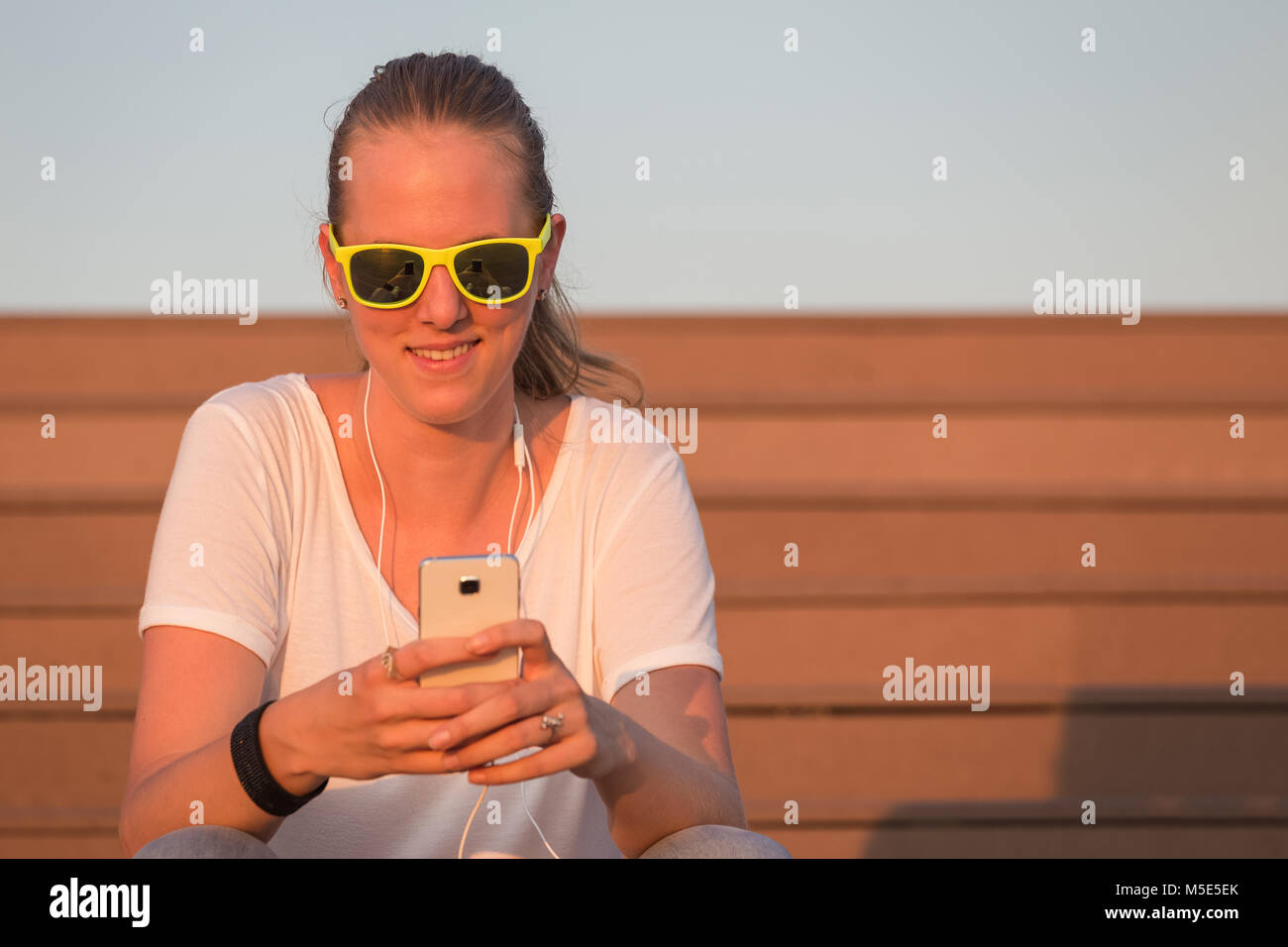Beautiful modern female siting on stairs and holding smart phone ...