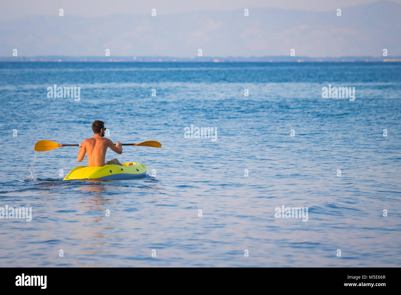 Rear view of man paddles yellow kayak in the ocean. Sport and ...