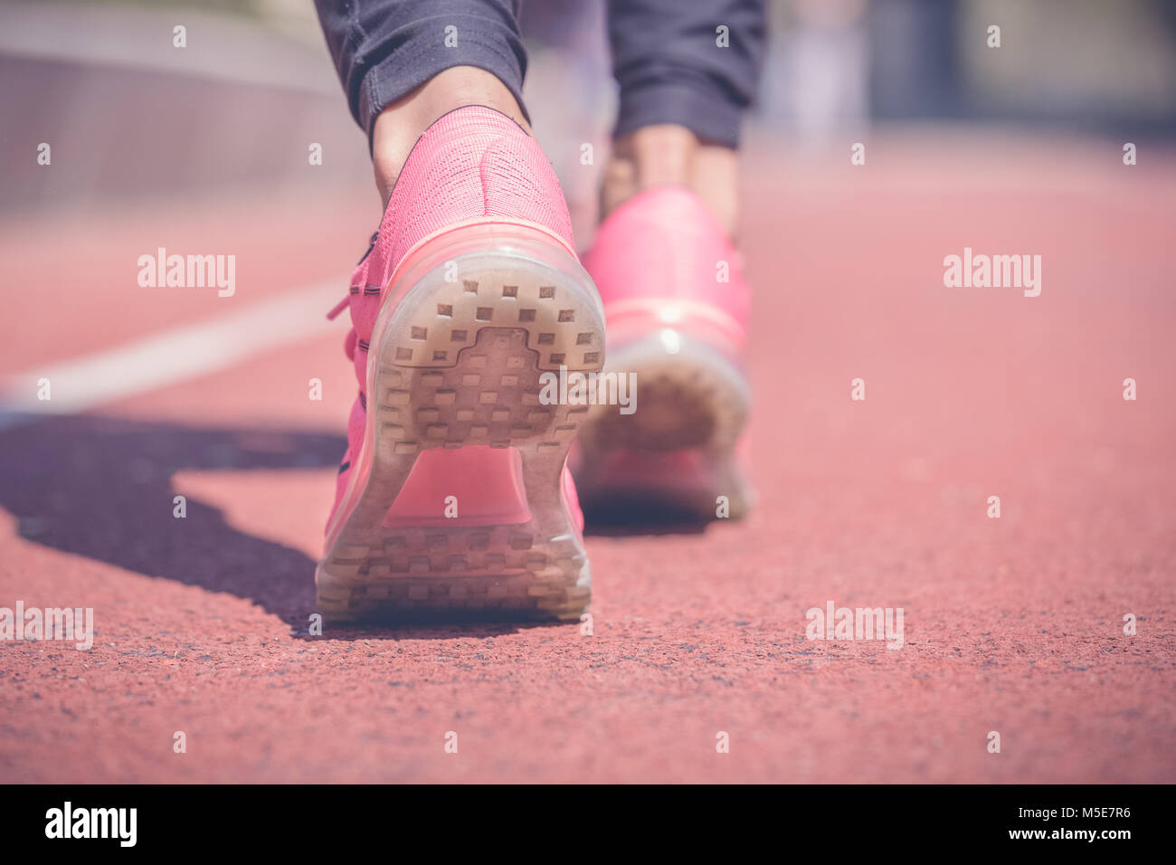 Back side view close up shot of female feet with sneakers on the red ...
