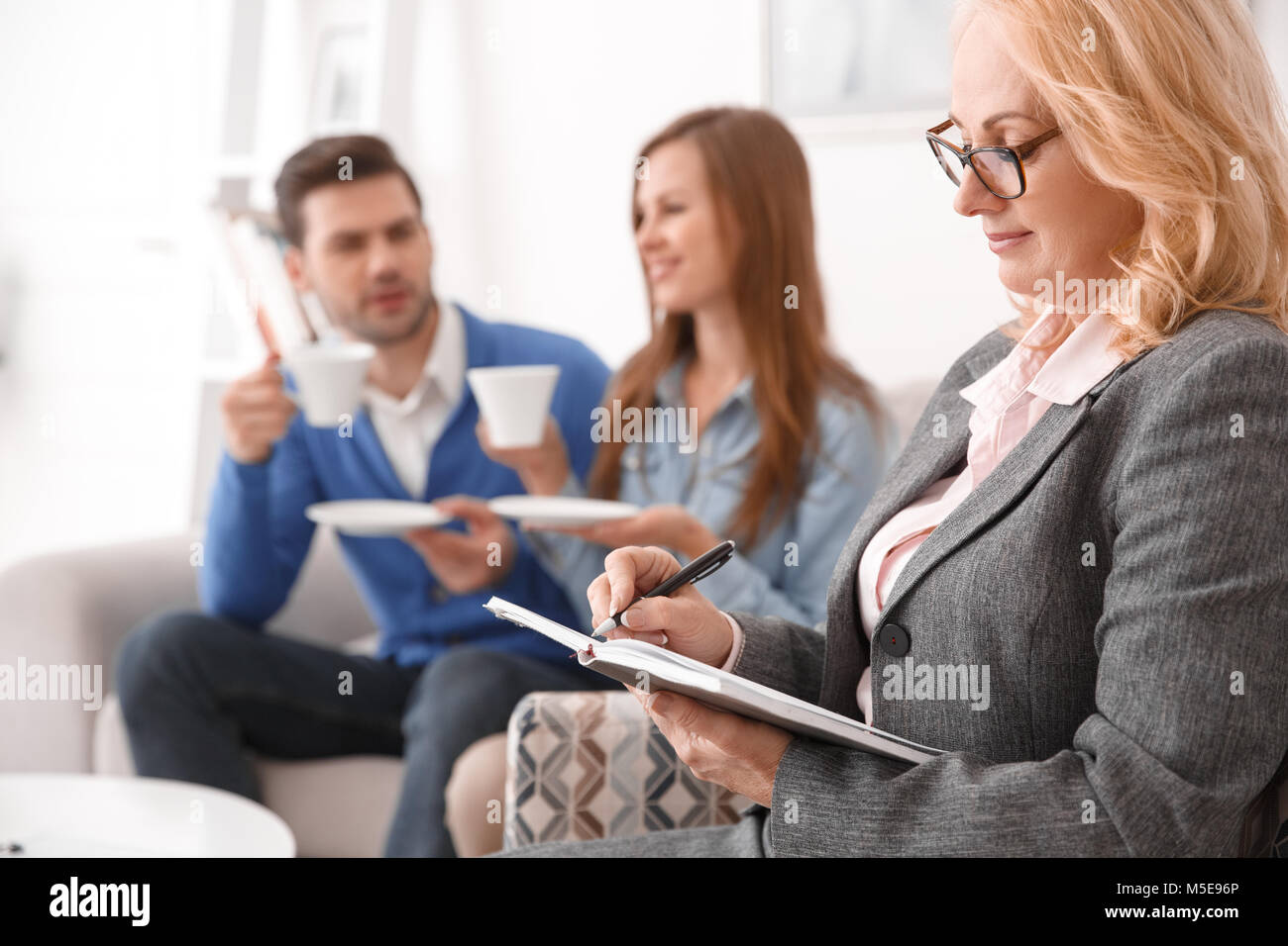 Couple at real estate sales office with agent taking notes in planner ...