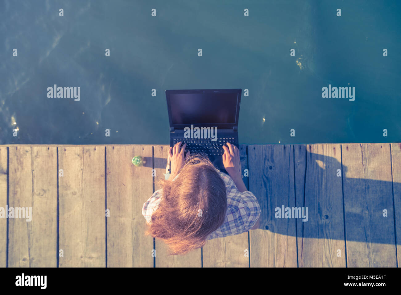 Top down perspective of female sitting on pier and working on laptop ...