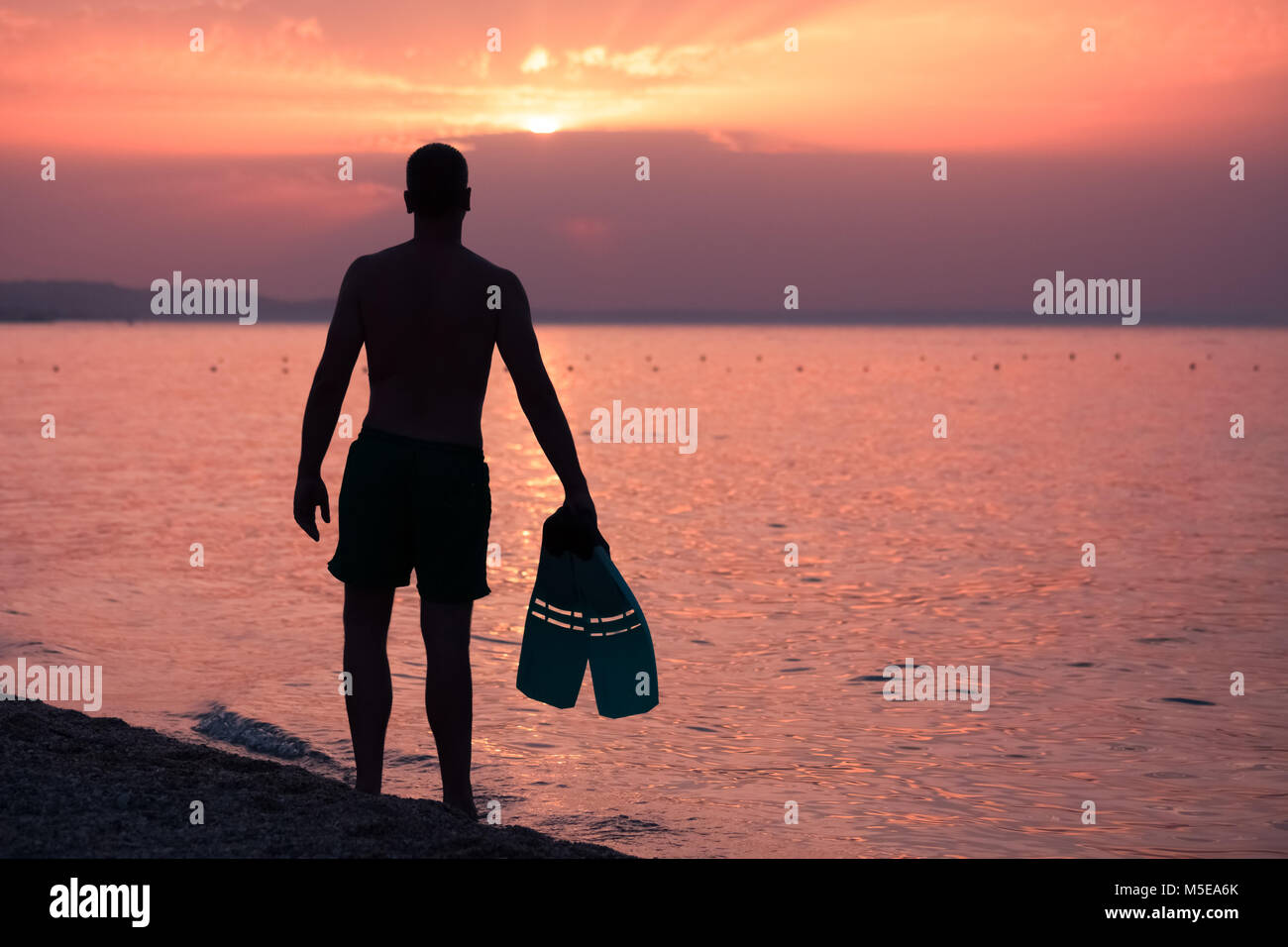 Silhouette of swimmer holding flippers on beach during the sunset over ...
