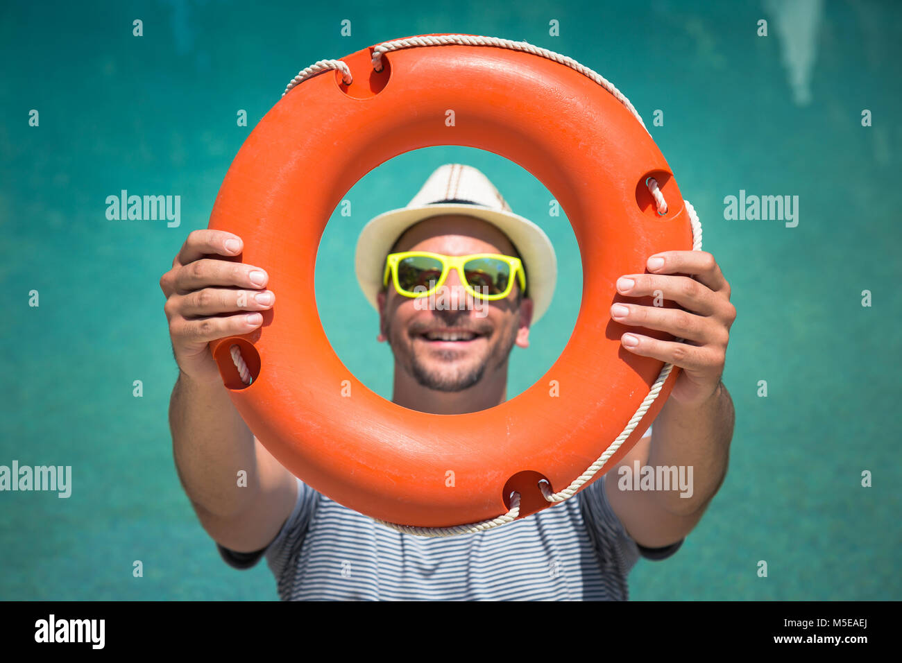 Portrait of young man showing and looking through lifebuoy outdoors ...