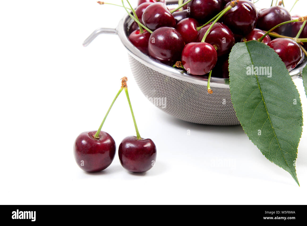 Steel colander with ripe berries of red sweet cherry and several ...