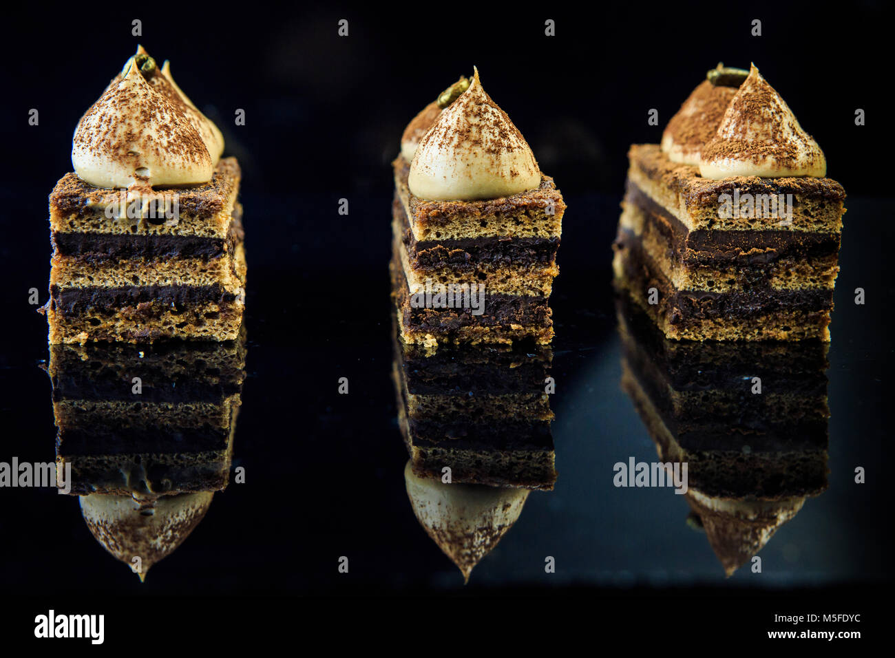 three chocolate opera cake slices decorated with white cream on black ...
