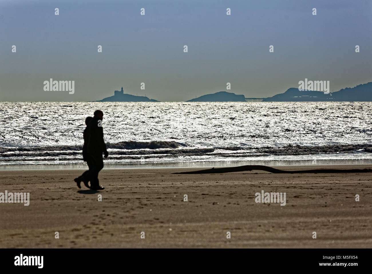 Pictured: A couple walk on the beach overlooking Mumbles at Swansea ...