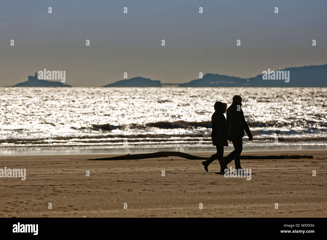 Pictured: A couple walk on the beach overlooking Mumbles at Swansea ...