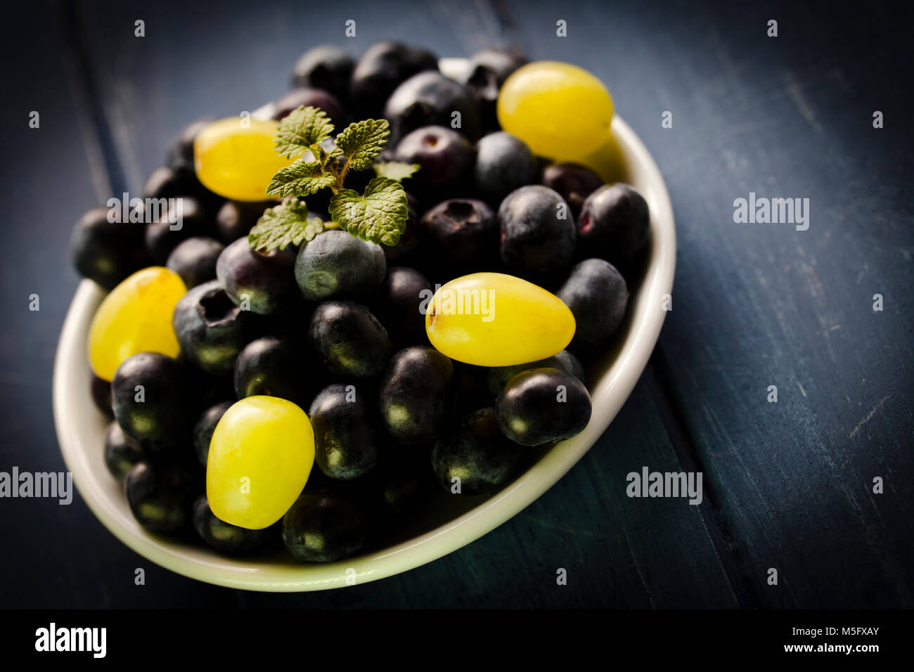 Vibrant image of two fruits; blueberries and grapes on wooden base with ...