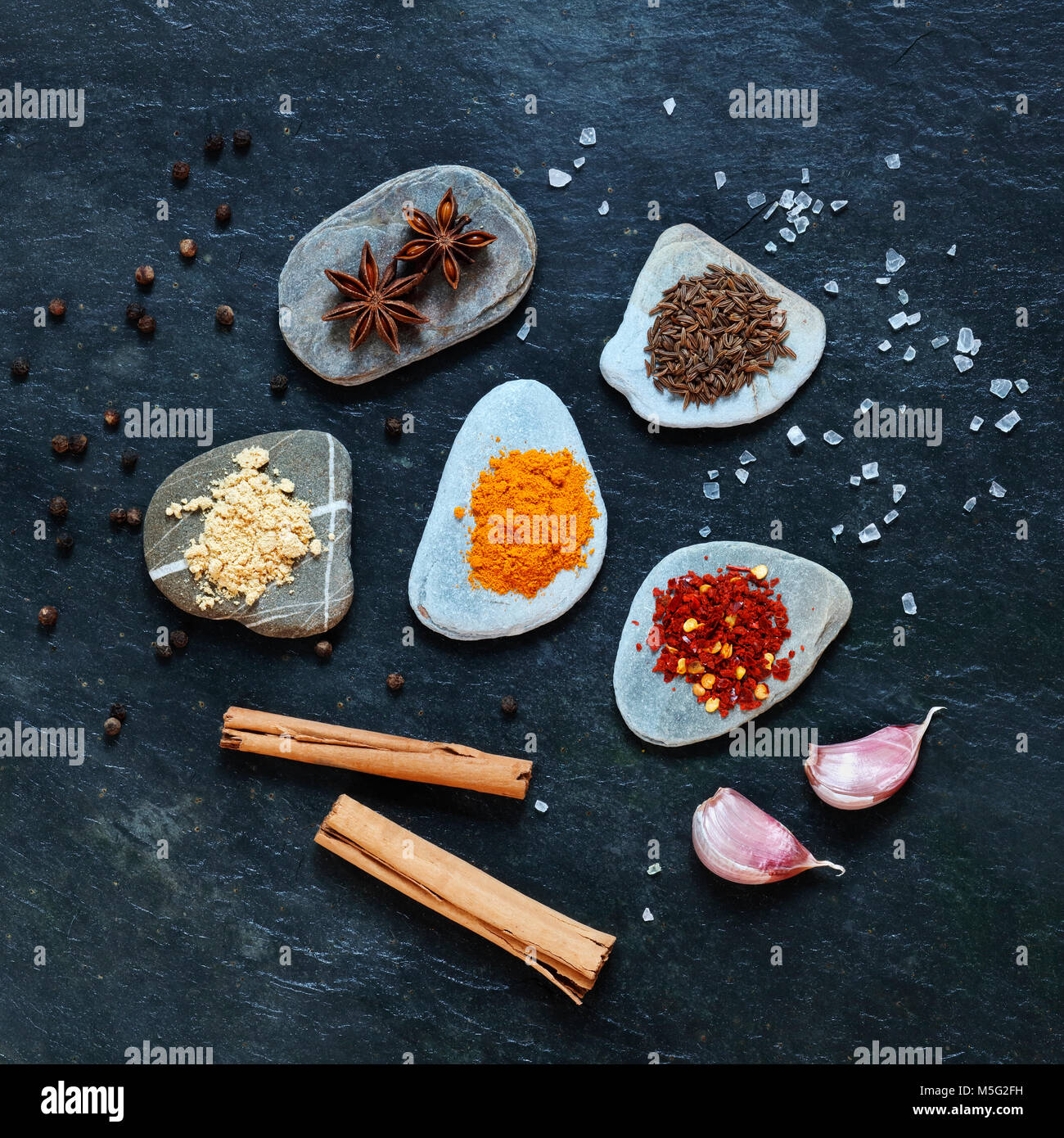 Colorful spices on pebbles in center group with cinnamon sticks, garlic ...