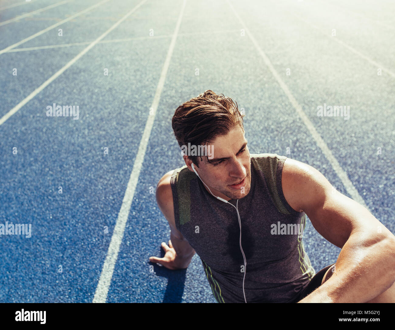 Close up of an athlete sitting on a running track listening to music ...