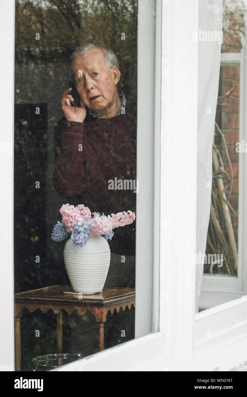 Senior man is looking out from his window into the street and is ...