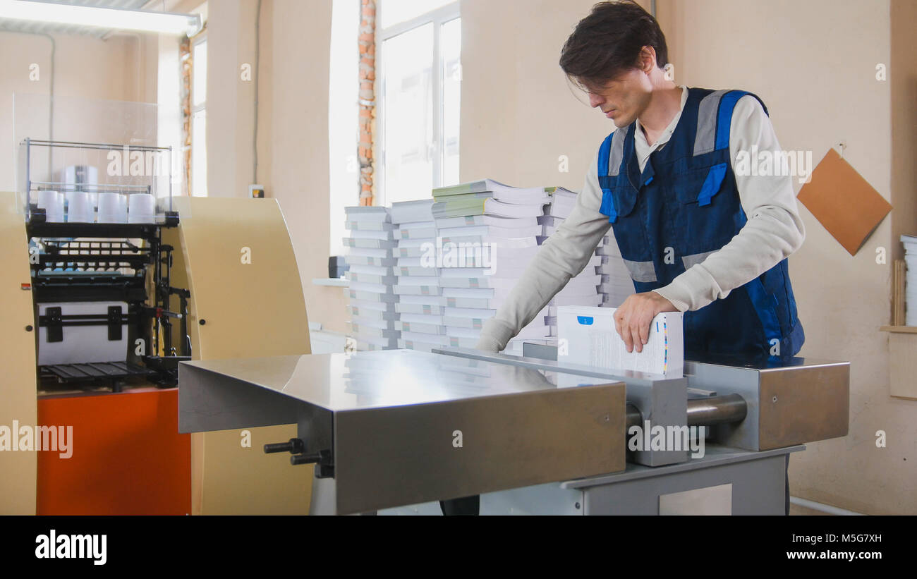 Printing process - worker inserts paper sheets in industrial press ...