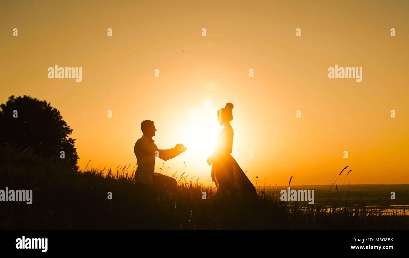 Romantic Silhouette of Man Getting Down on his Knee and Proposing to ...