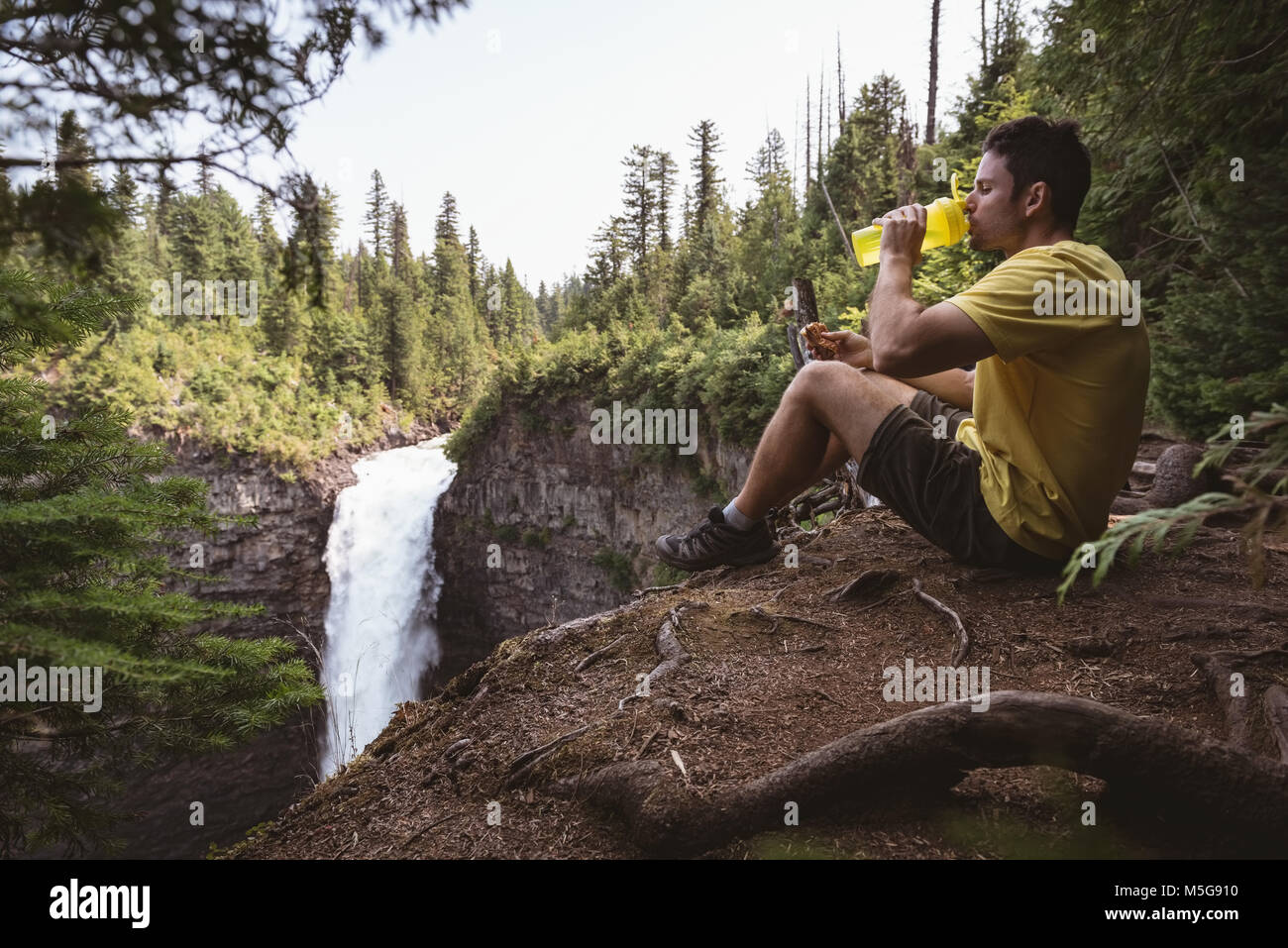 Man sitting near waterfall and drinking water Stock Photo - Alamy