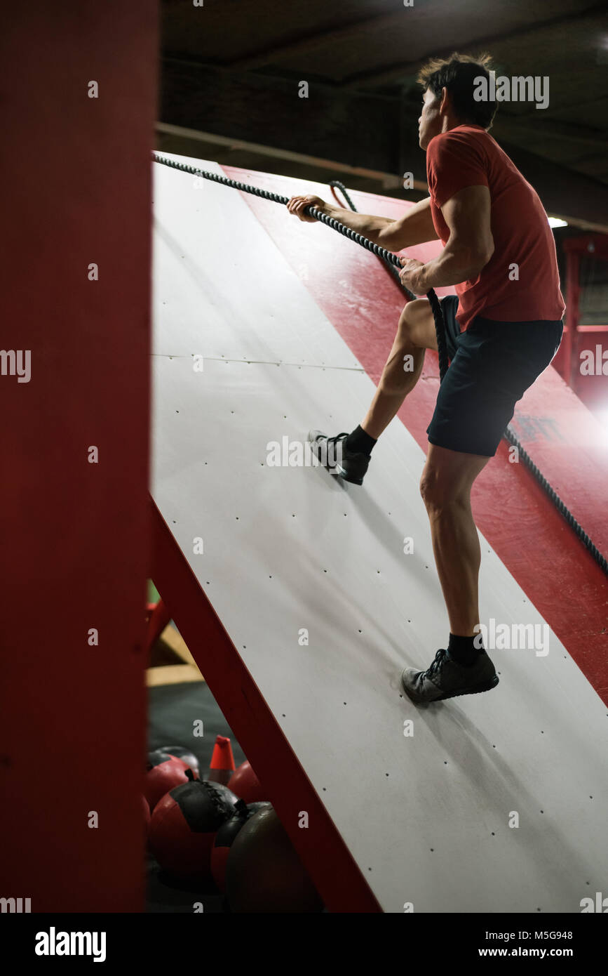 Muscular man climbing an inclined wall with rope Stock Photo - Alamy