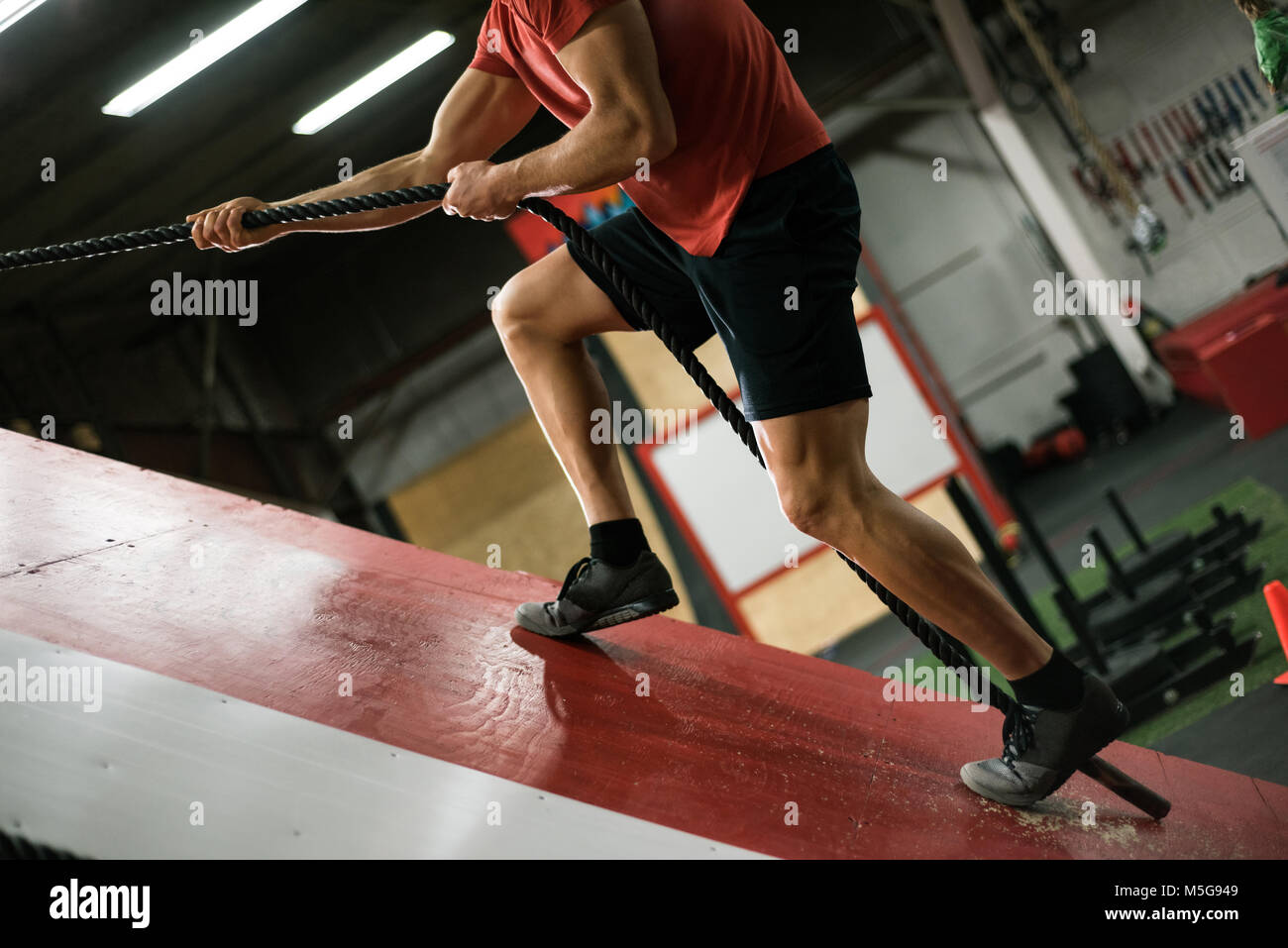 Muscular man climbing an inclined wall with rope Stock Photo - Alamy