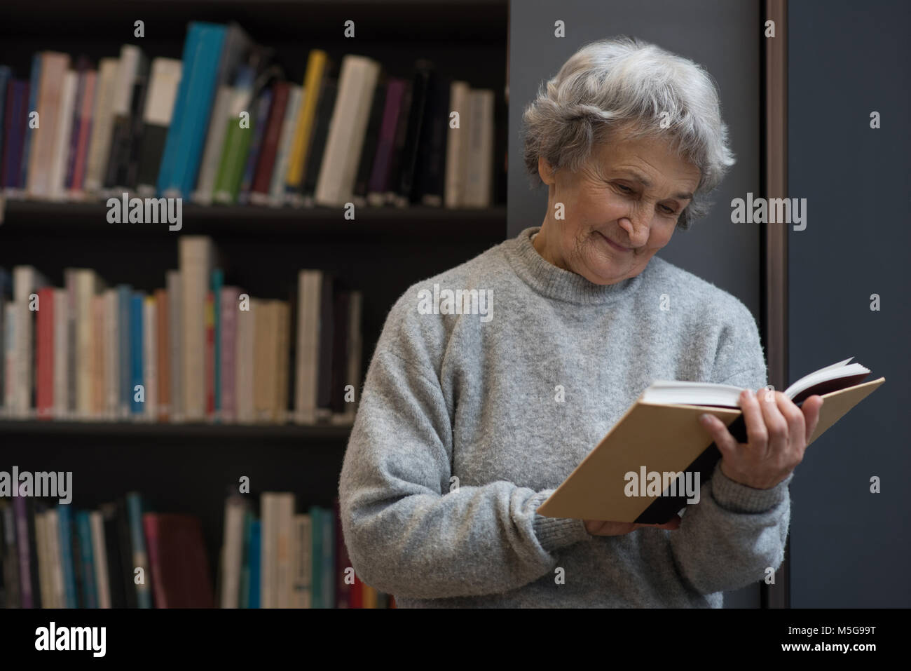 Senior woman reading a book in library Stock Photo - Alamy