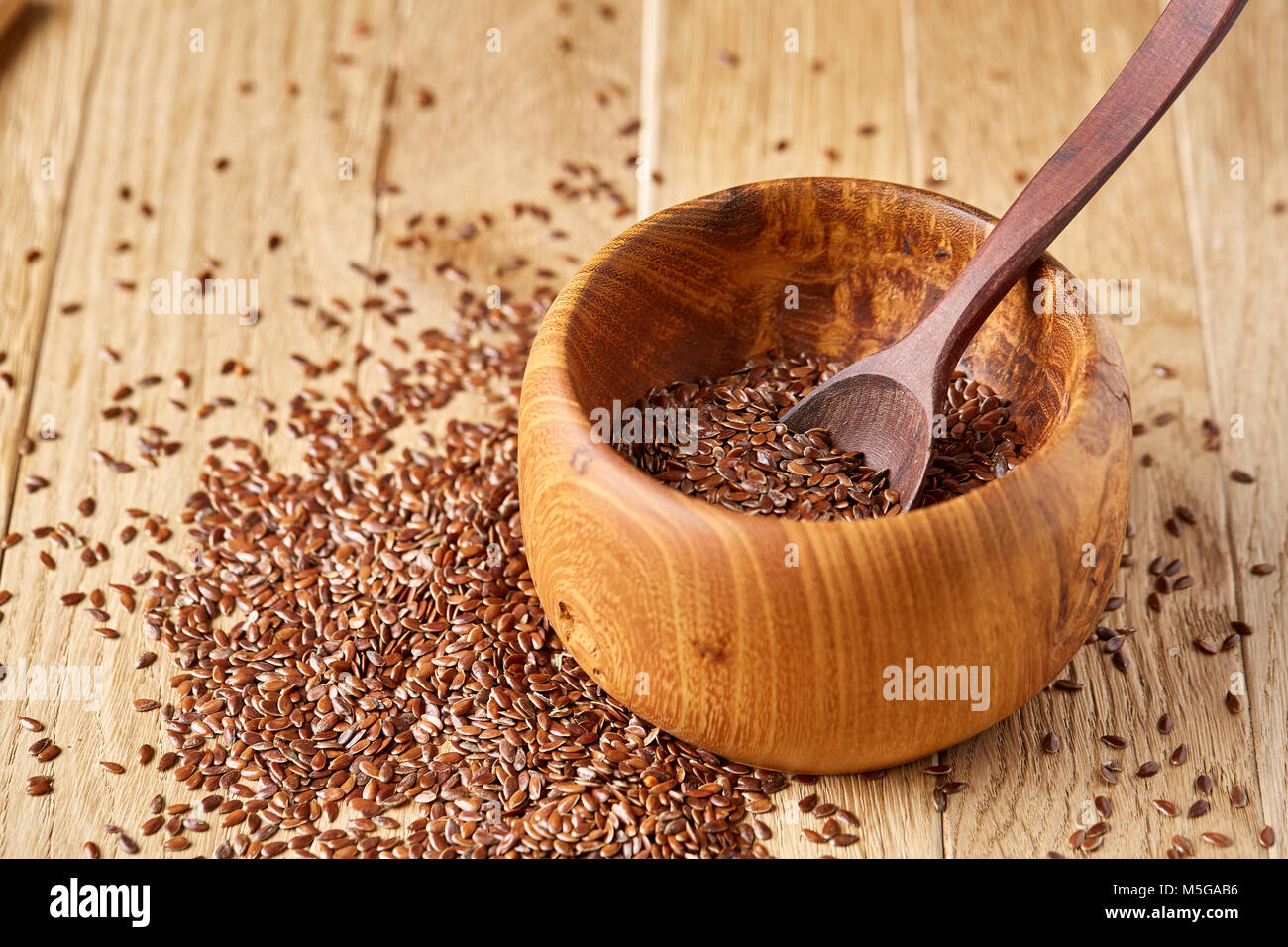 Top view close-up picture of flax seeds in wooden bowl and spoon isolated on brown rustic wooden ...