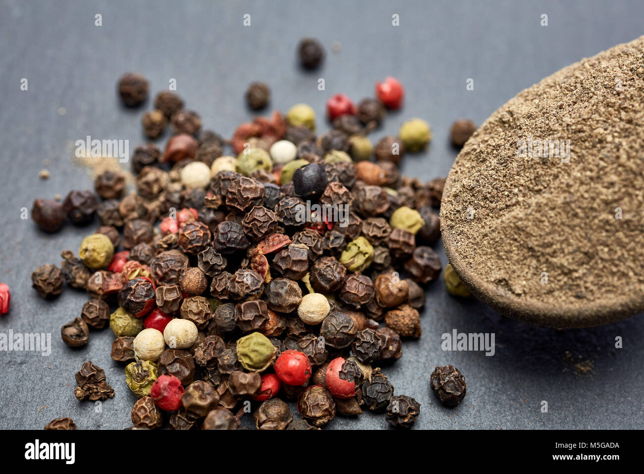 Top view of a wooden spoon full of grind black pepper powder surrounded ...