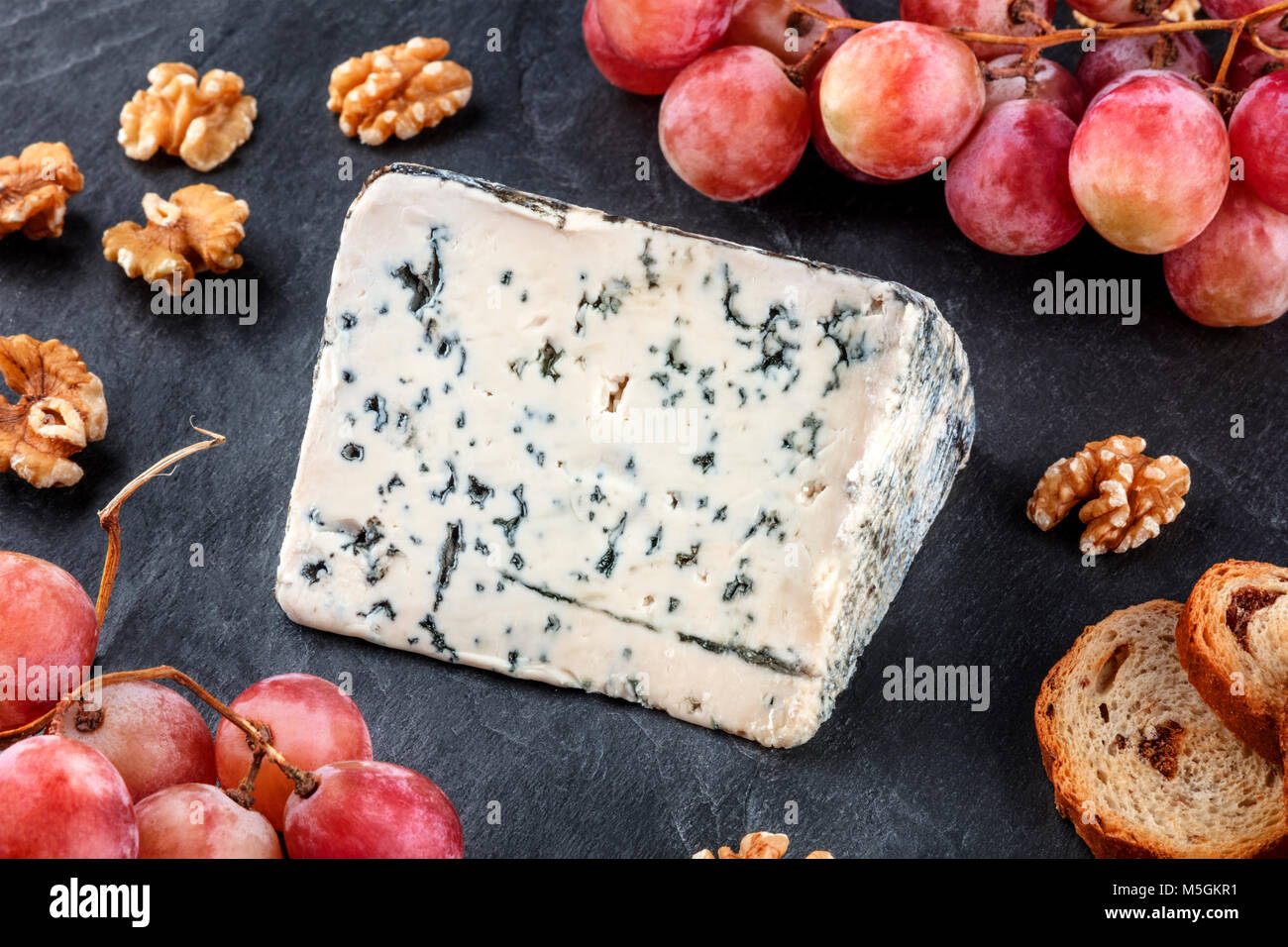 A photo of a piece of Gorgonzola cheese with vibrant grapes, slices of ...