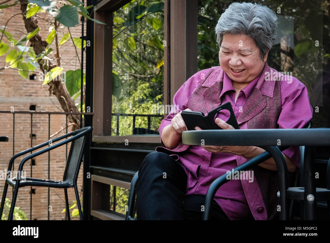 asian elder woman holding mobile phone on terrace. elderly female ...