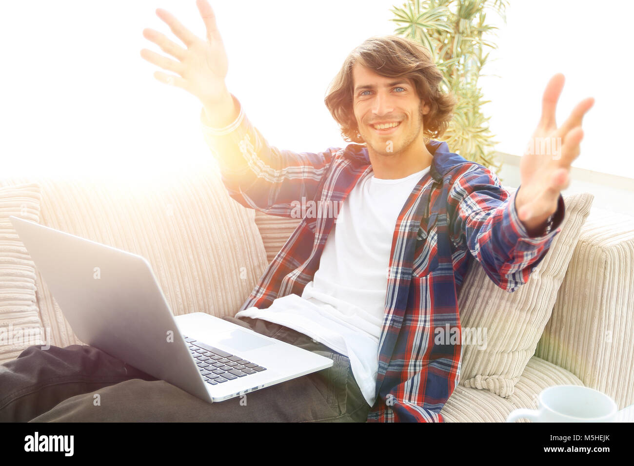 happy guy with laptop sitting on sofa and making a welcome gesture ...
