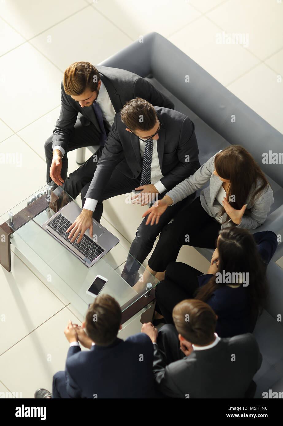 Young business team sitting and standing around the table and sharing ...