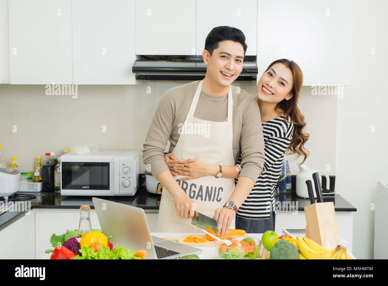 Portrait of happy asian young couple cooking together in the kitchen at ...