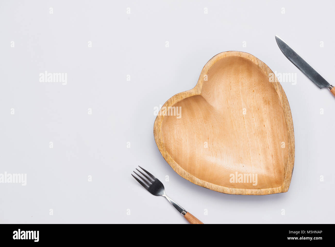 Wooden plate in shape of heart, table knife and fork on white ...
