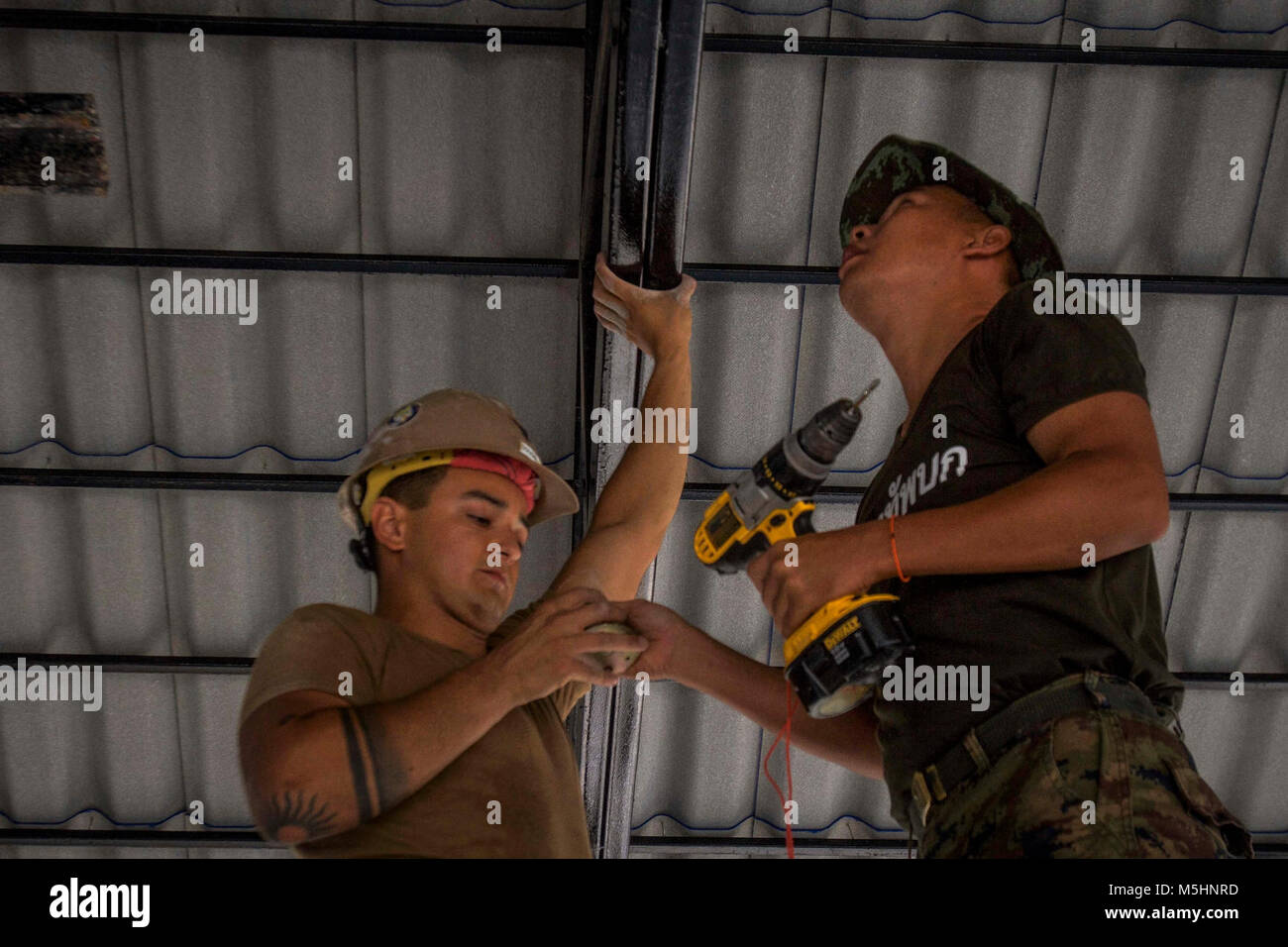 A U.S. Navy sailor helps a Royal Thai Navy sailor put up rafters for a ...