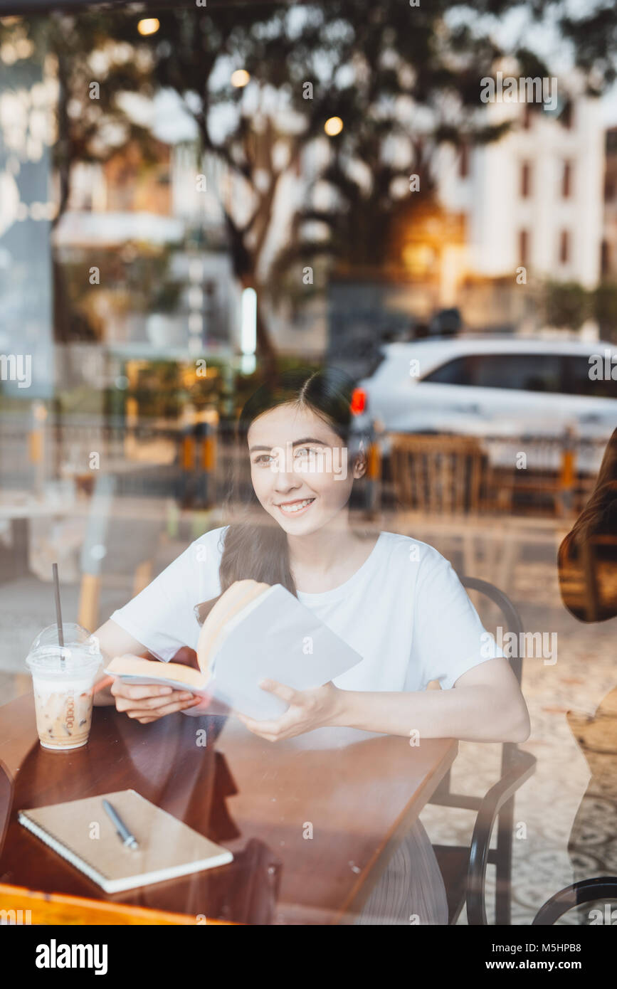 Asian woman reading book vintage color tone. Viewed through window of ...