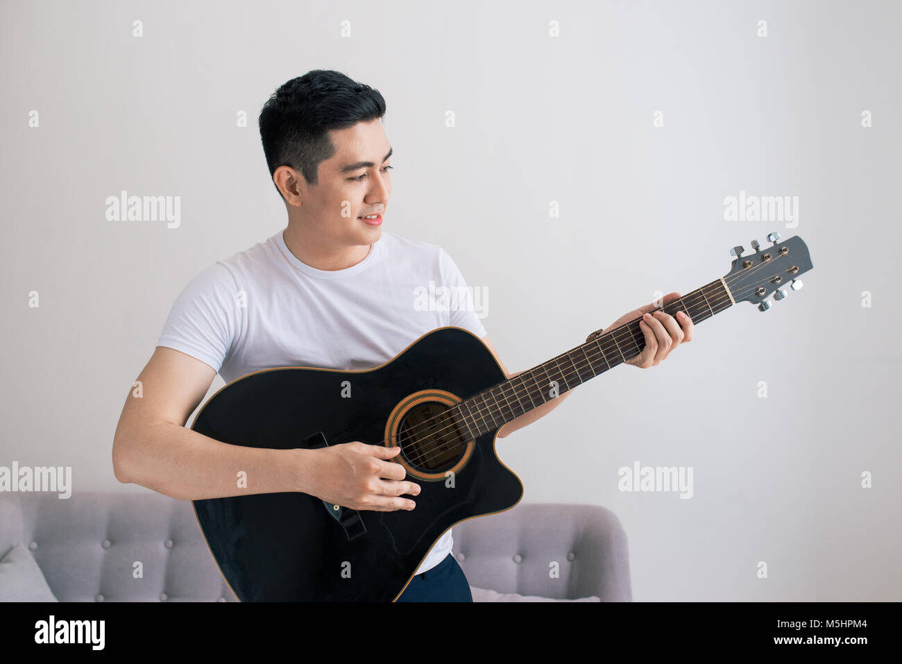 Handsome asian man playing on the guitar on the couch at home Stock ...