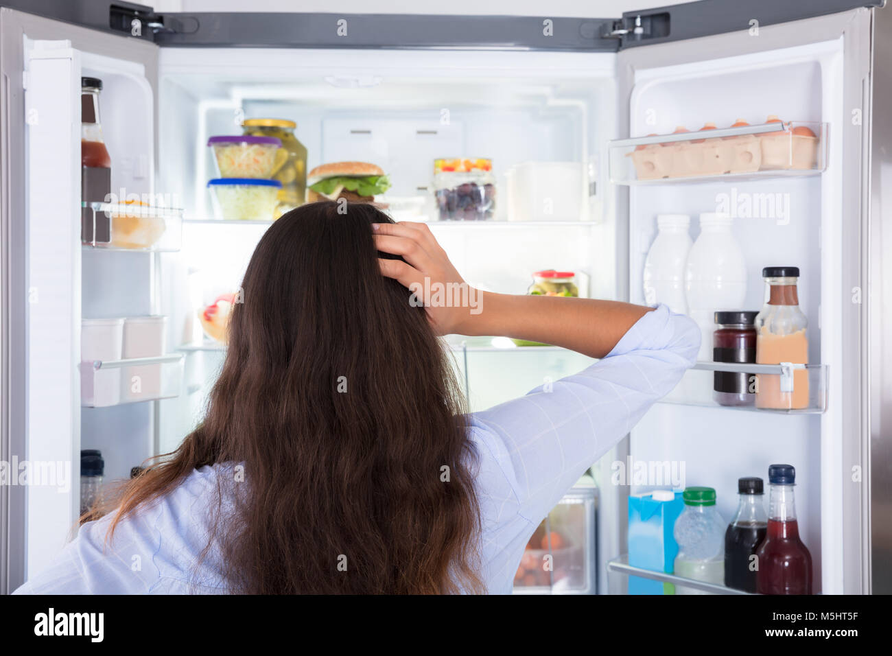 Rear View Of A Confused Young Woman Looking In Open Refrigerator Stock ...