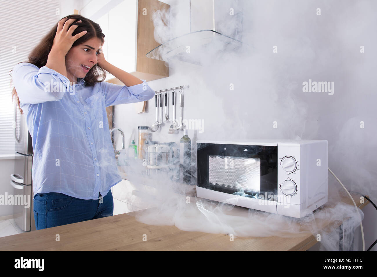 Unhappy Young Woman Looking At Smoke Emitting Through Microwave Oven In ...