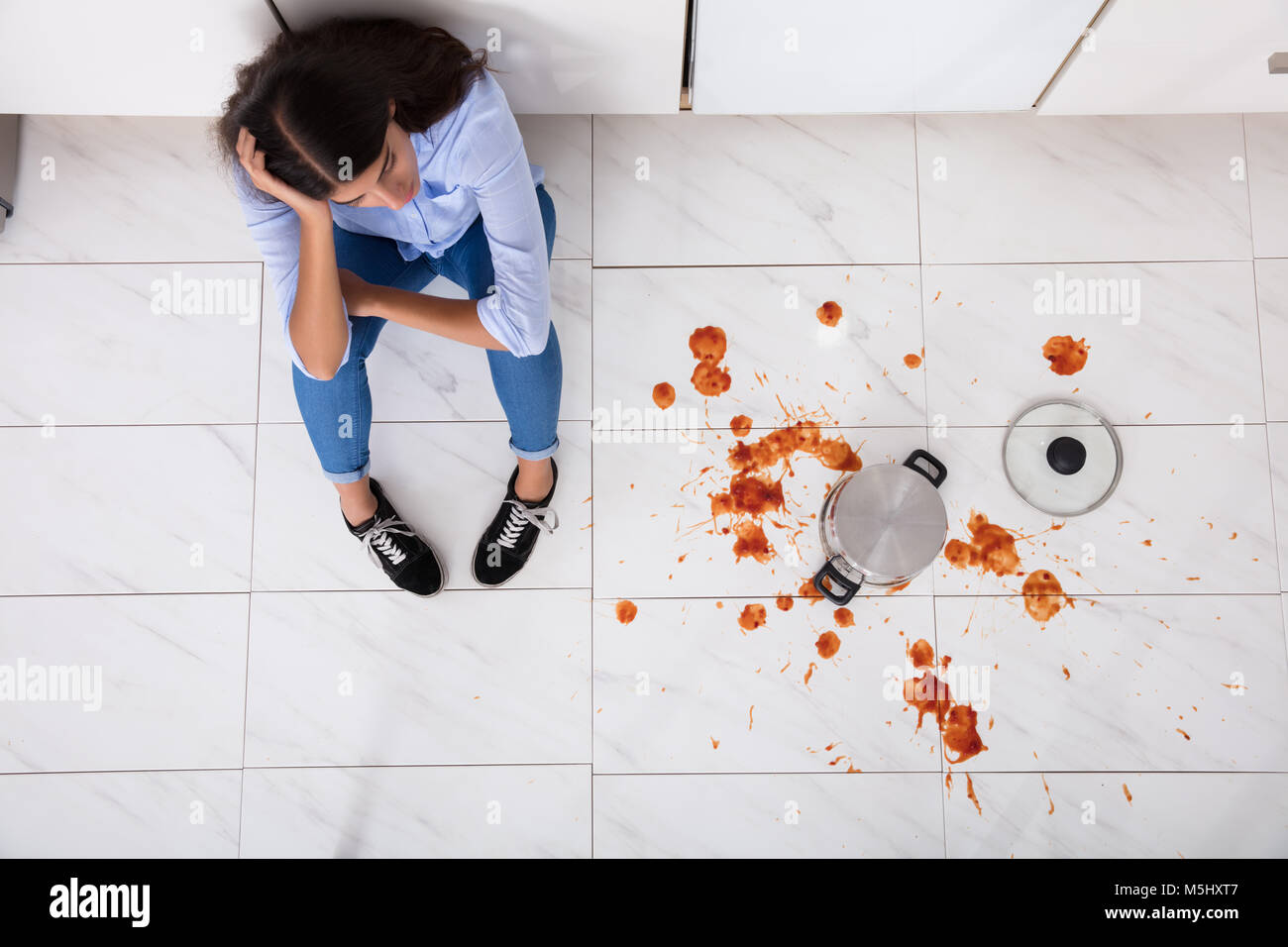 Unhappy Woman Sitting On Kitchen Floor With Spilled Food In Kitchen ...