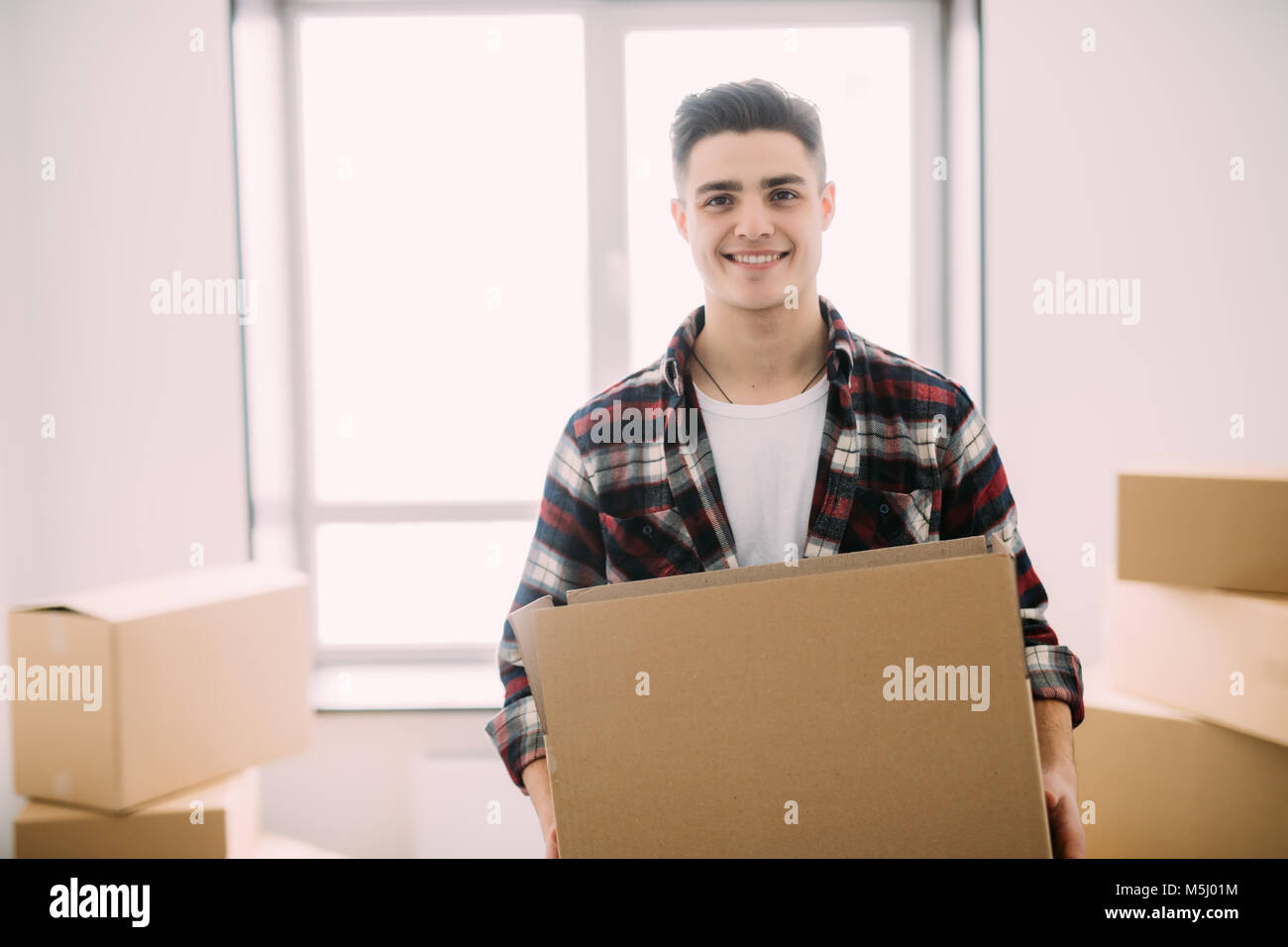 Portrait of a smiling man carrying boxes in new house Stock Photo - Alamy