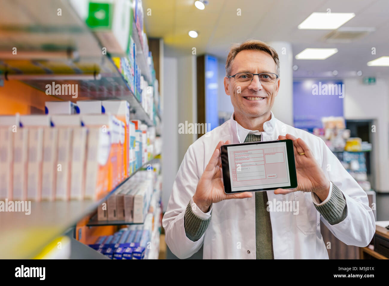 Portrait of smiling pharmacist in pharmacy holding tablet with digital ...