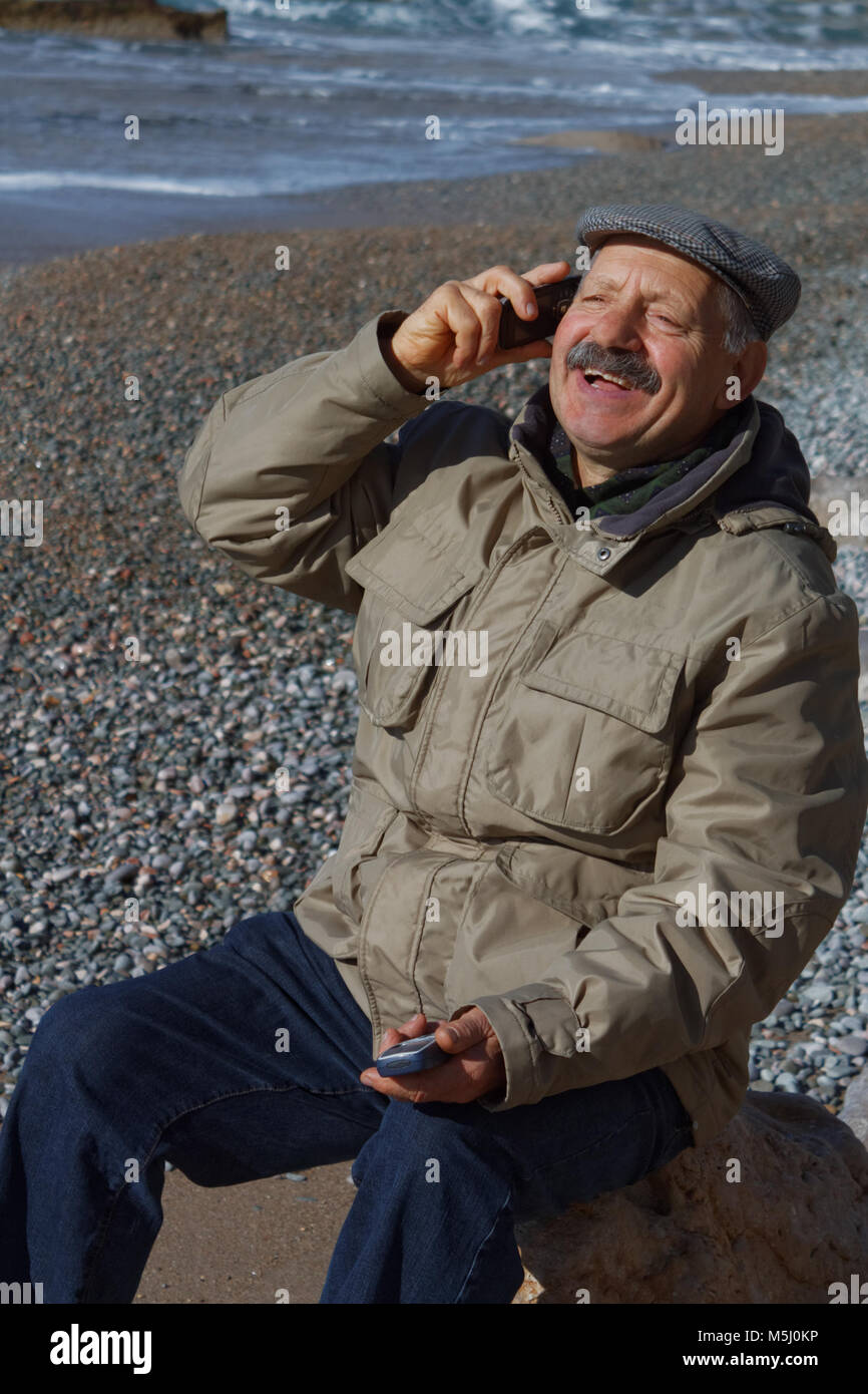 Senior man on the beach talking by mobile phone and holding a second ...