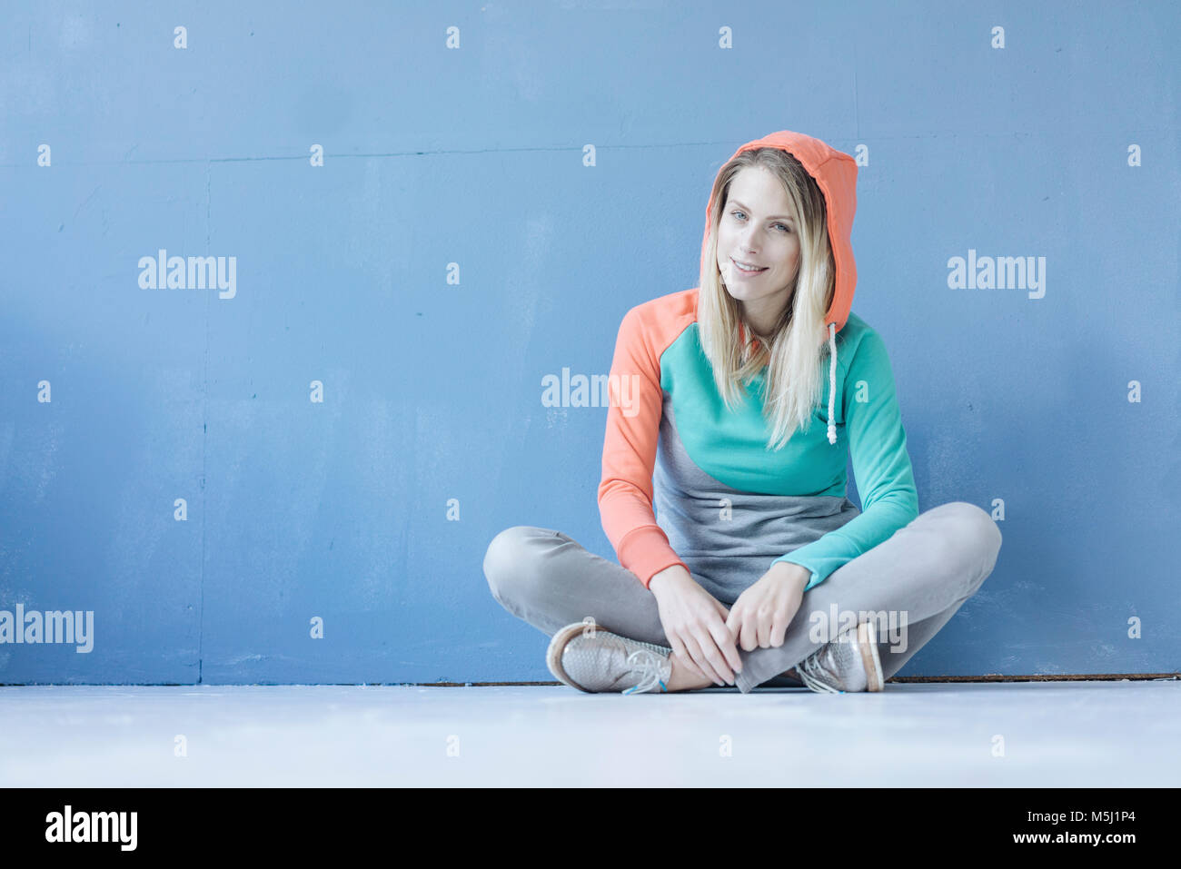Portrait of smiling woman wearing hooded jacket sitting on the floor in ...