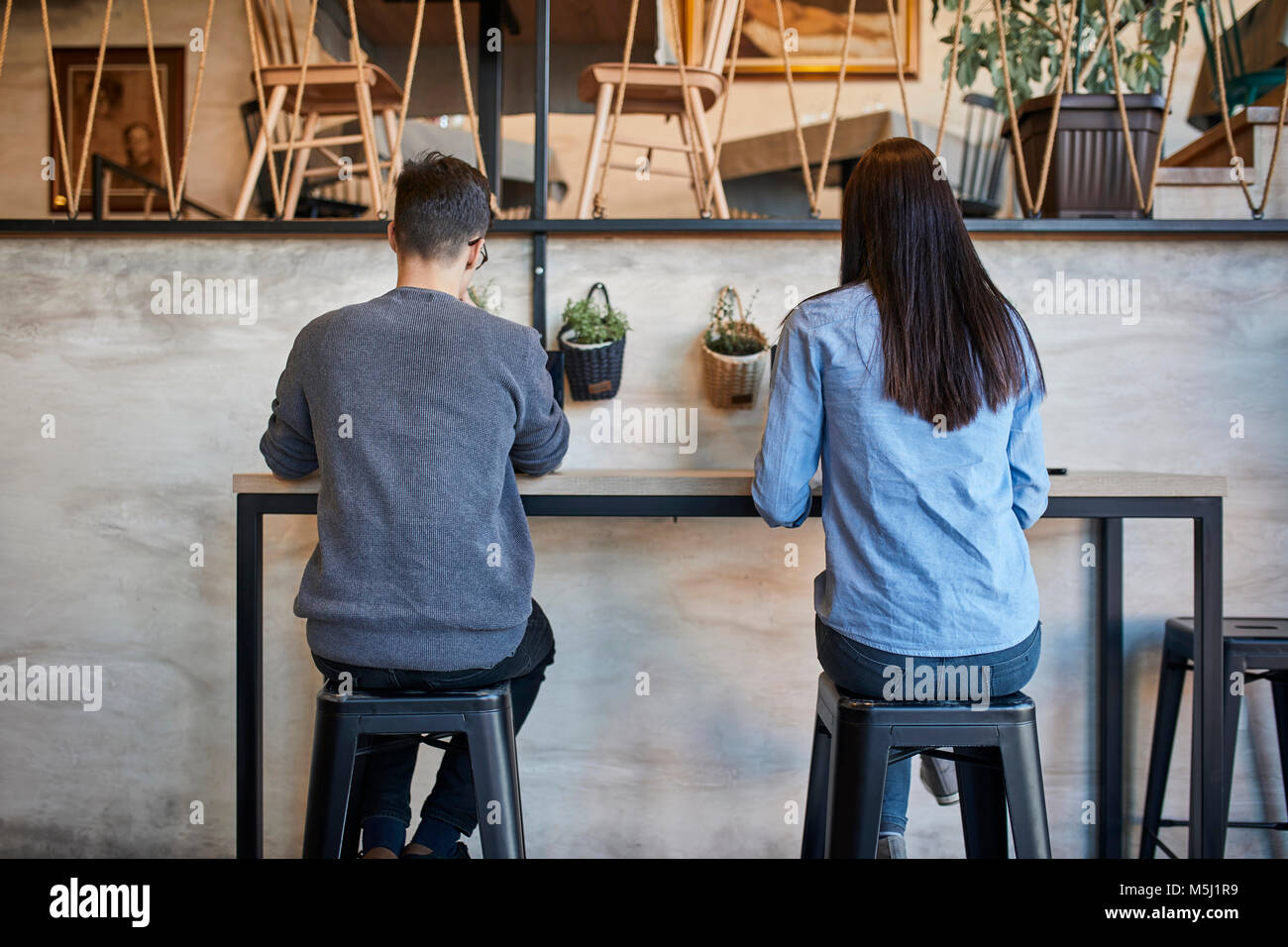 Rear view of young woman and man sitting in a cafe Stock Photo - Alamy