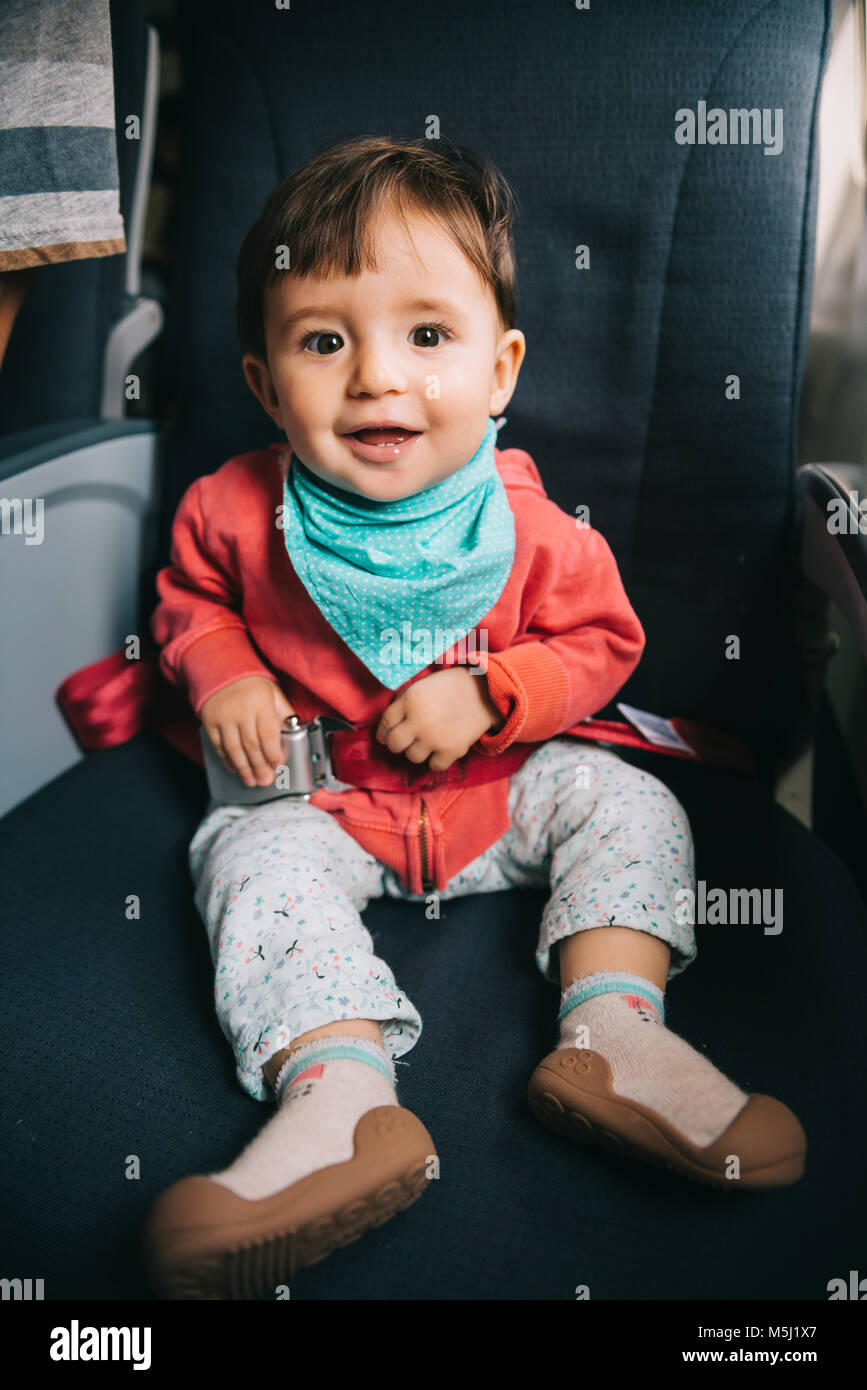 Baby sitting on a plane next to the window with a seat belt fasten ...