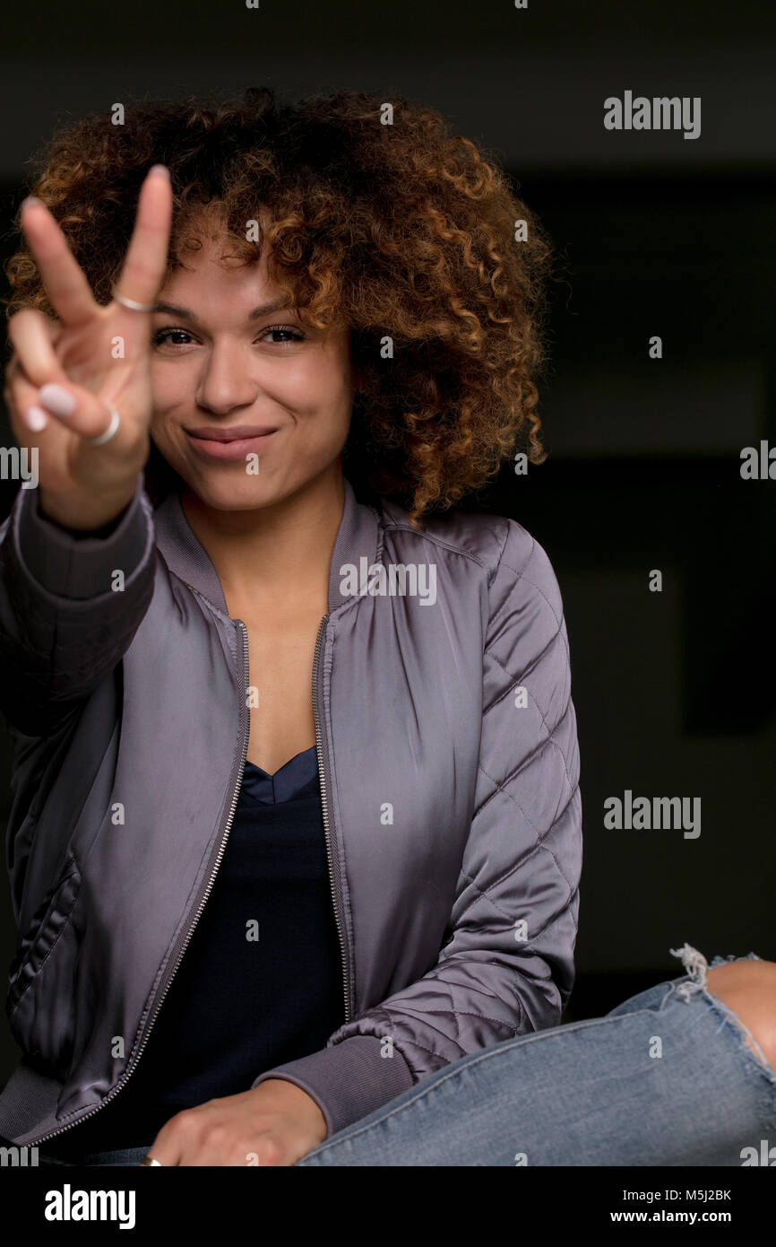 Portrait of smiling woman showing victory sign Stock Photo - Alamy