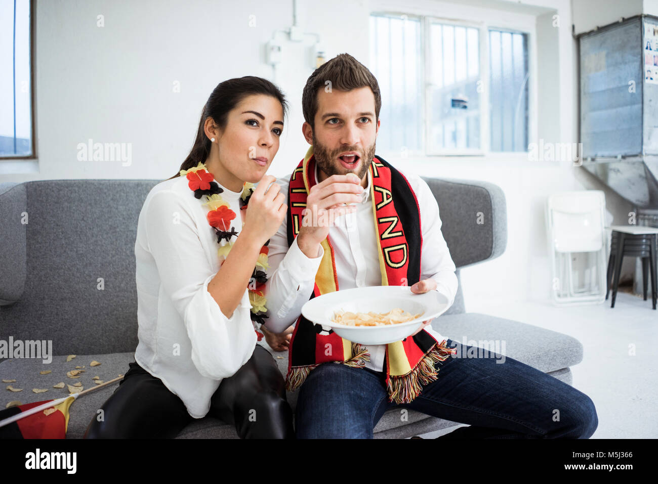 German football fan couple sitting on couch eating chips and watching ...