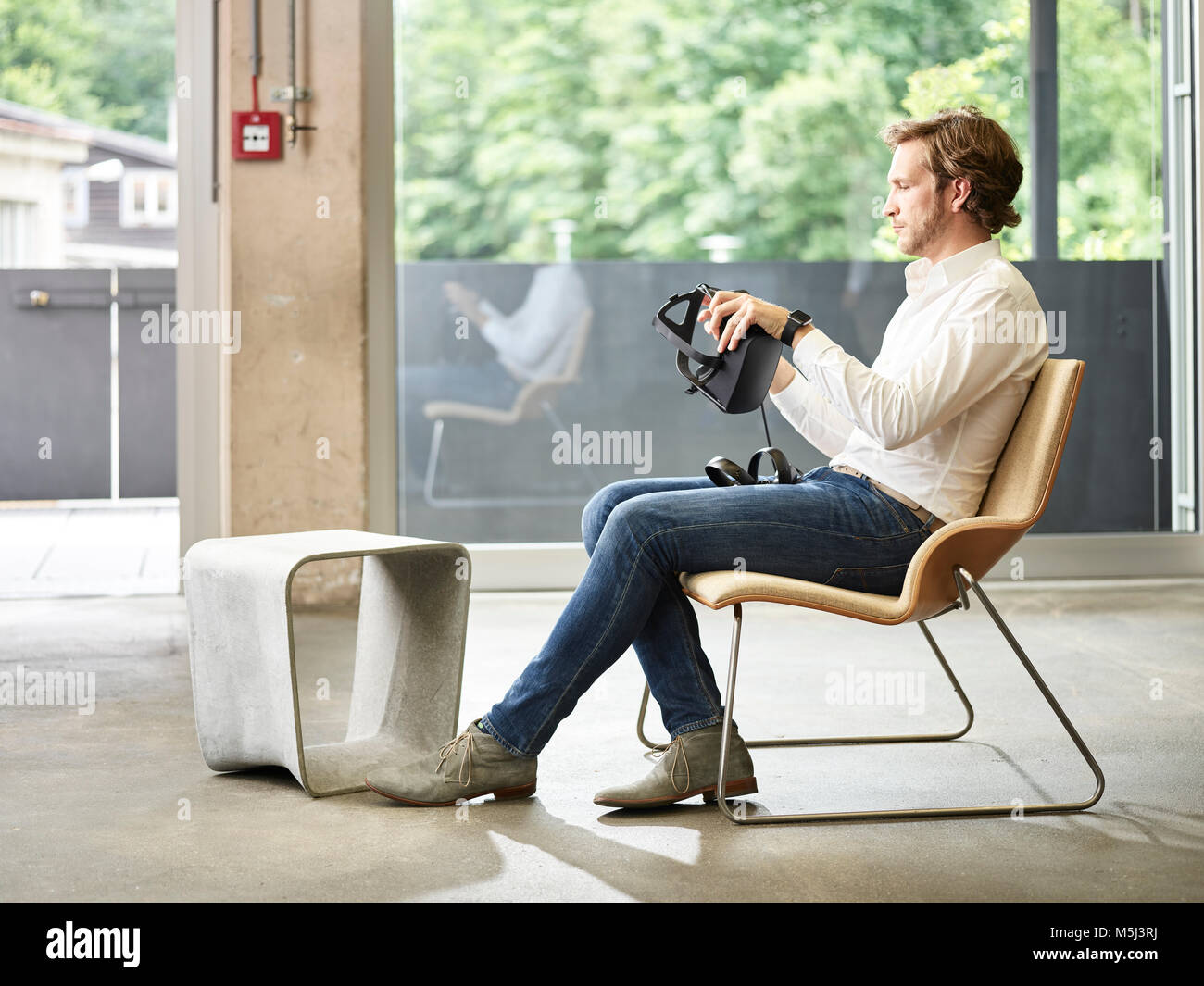Man holding VR glasses sitting on chair Stock Photo - Alamy