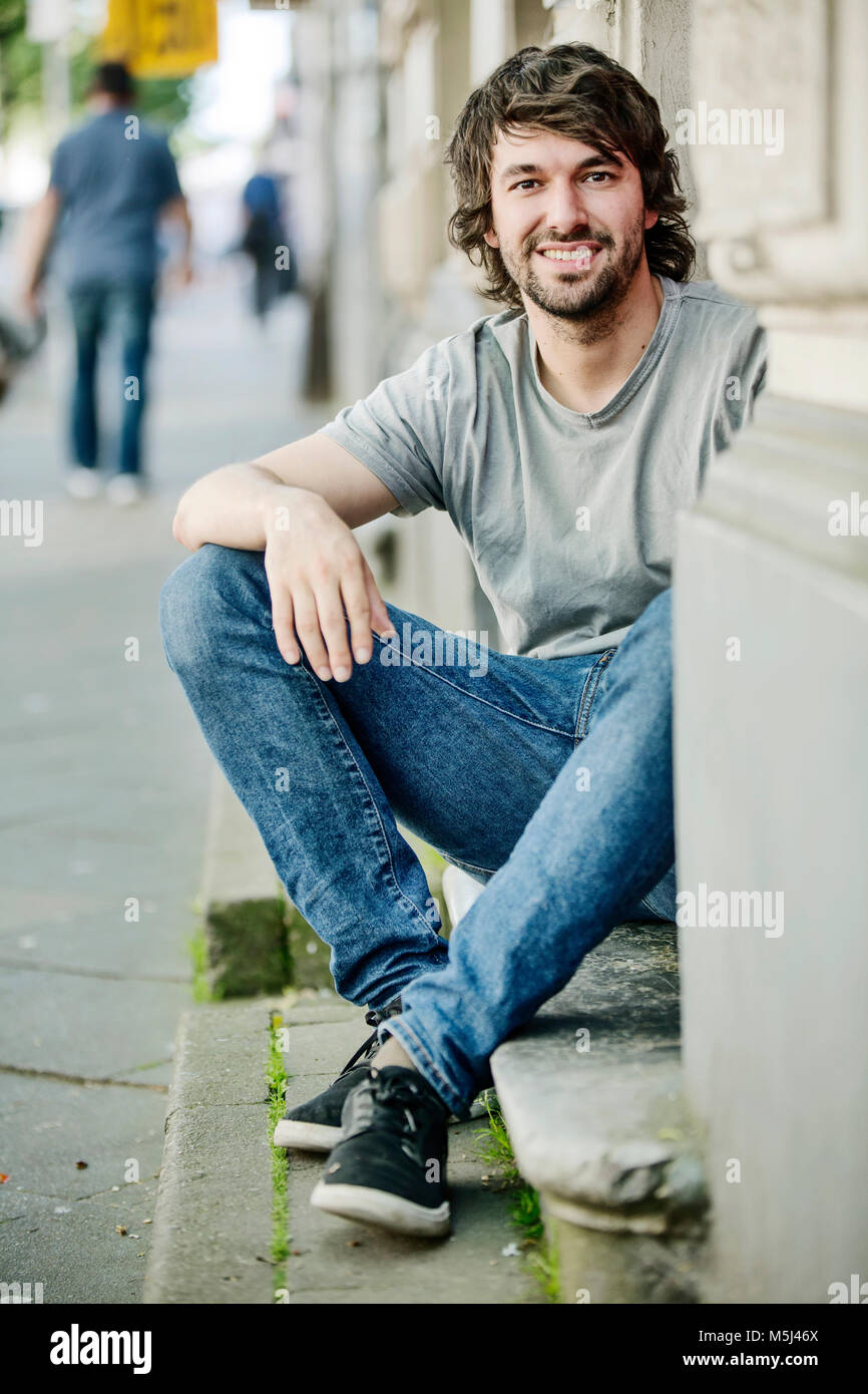 Portrait of smiling young man sitting on step outdoors Stock Photo - Alamy